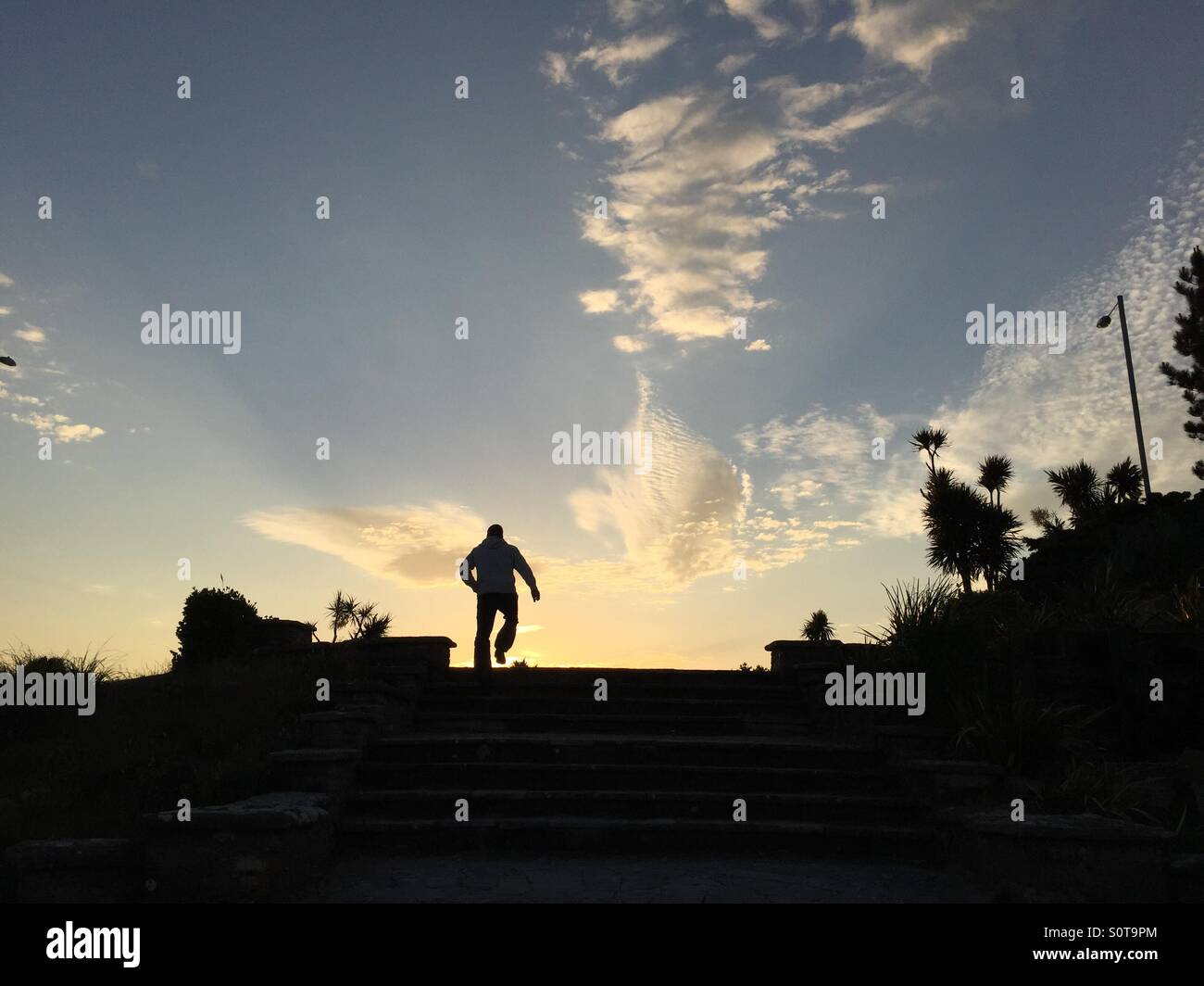 Man running up steps into sunset Stock Photo - Alamy