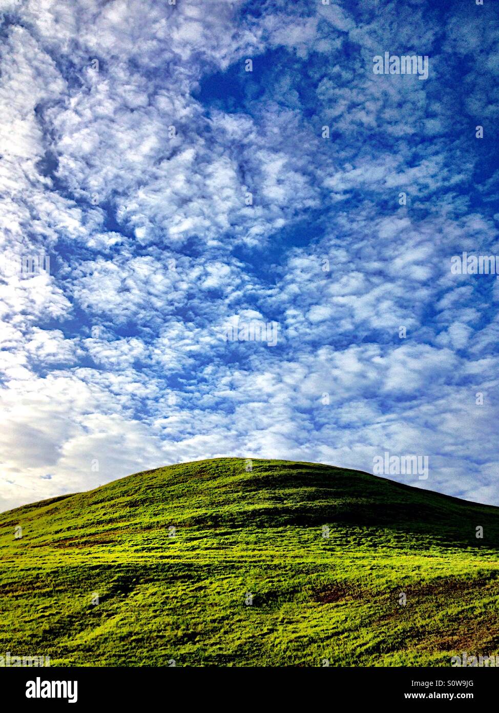 Light, broken clouds over a green, grassy hill Stock Photo - Alamy