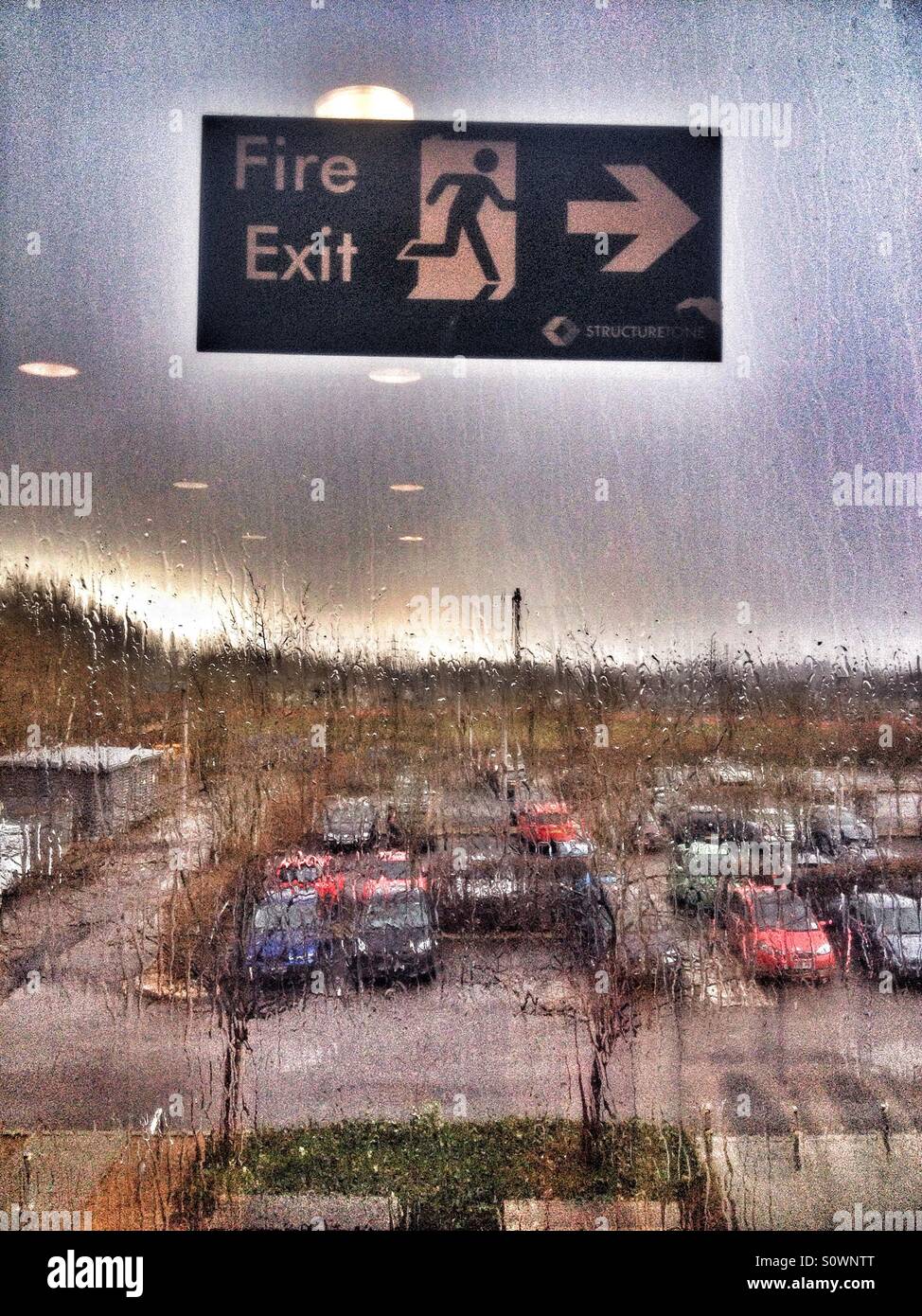 A fire exit sign on a window which overlooks a car park. Ran water ...