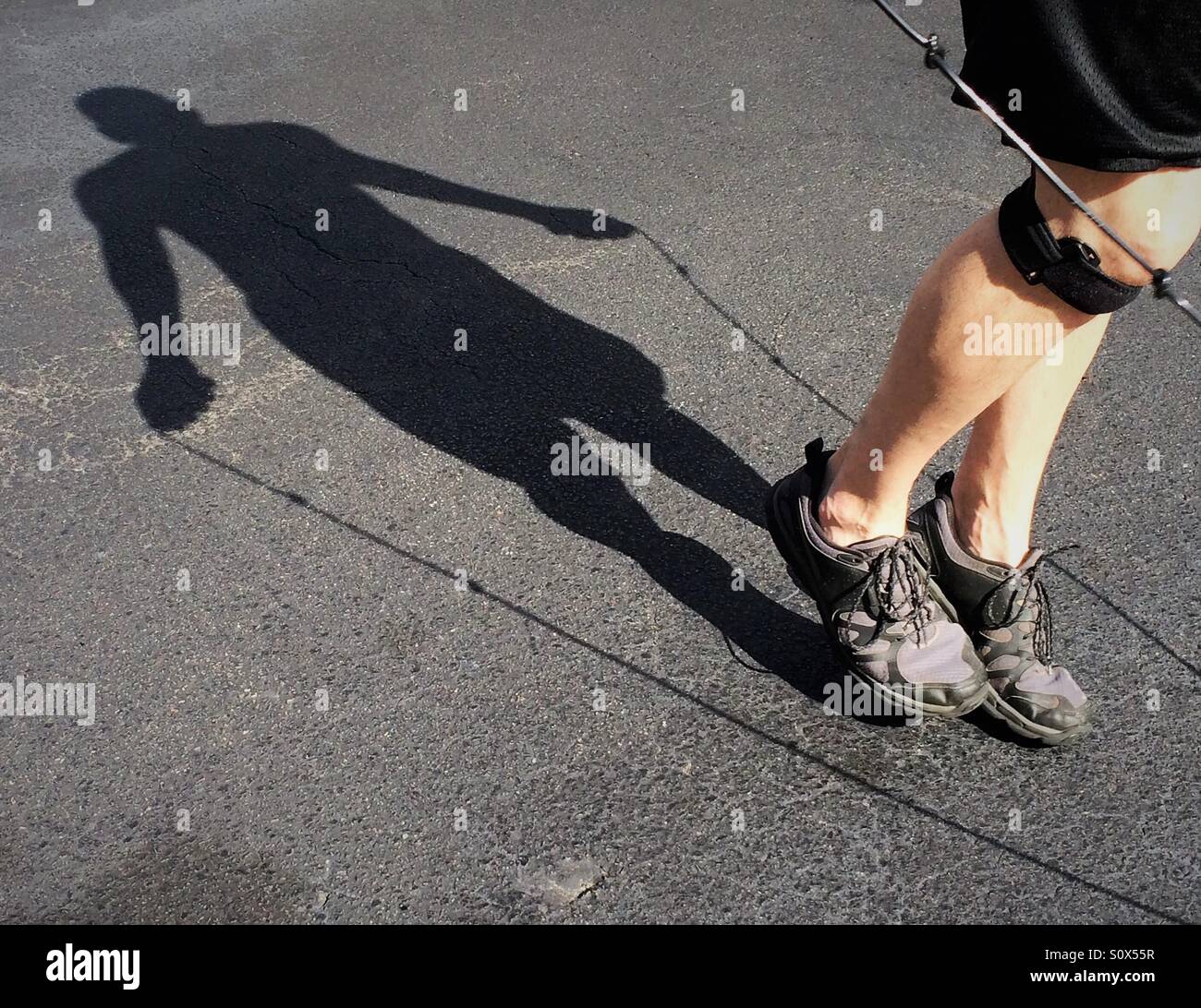 Shadow of a man jumping rope on black pavement Stock Photo - Alamy