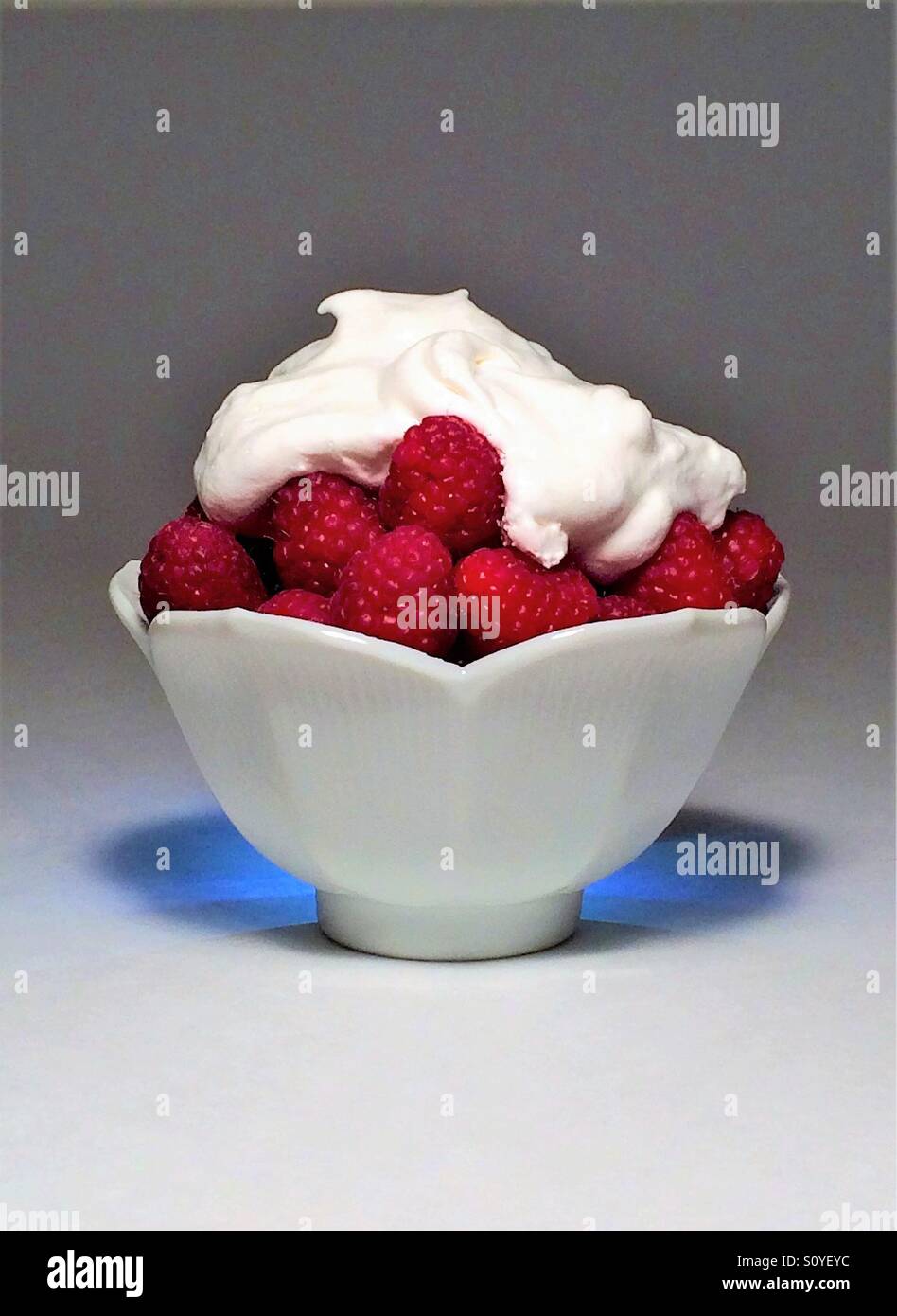 Raspberries with cream in a white bowl with white background and blue ...