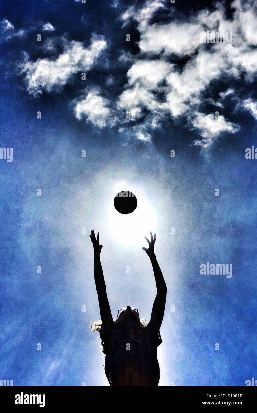 Young girl jumping up to catch ball in silhouette against blue sky ...