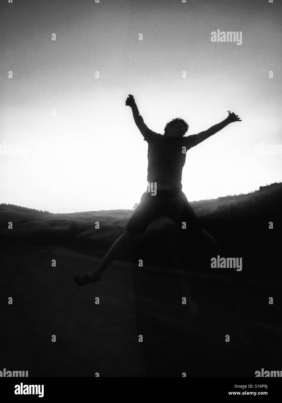 Silhouette of a young man jumping up in the air with arms up in the air ...