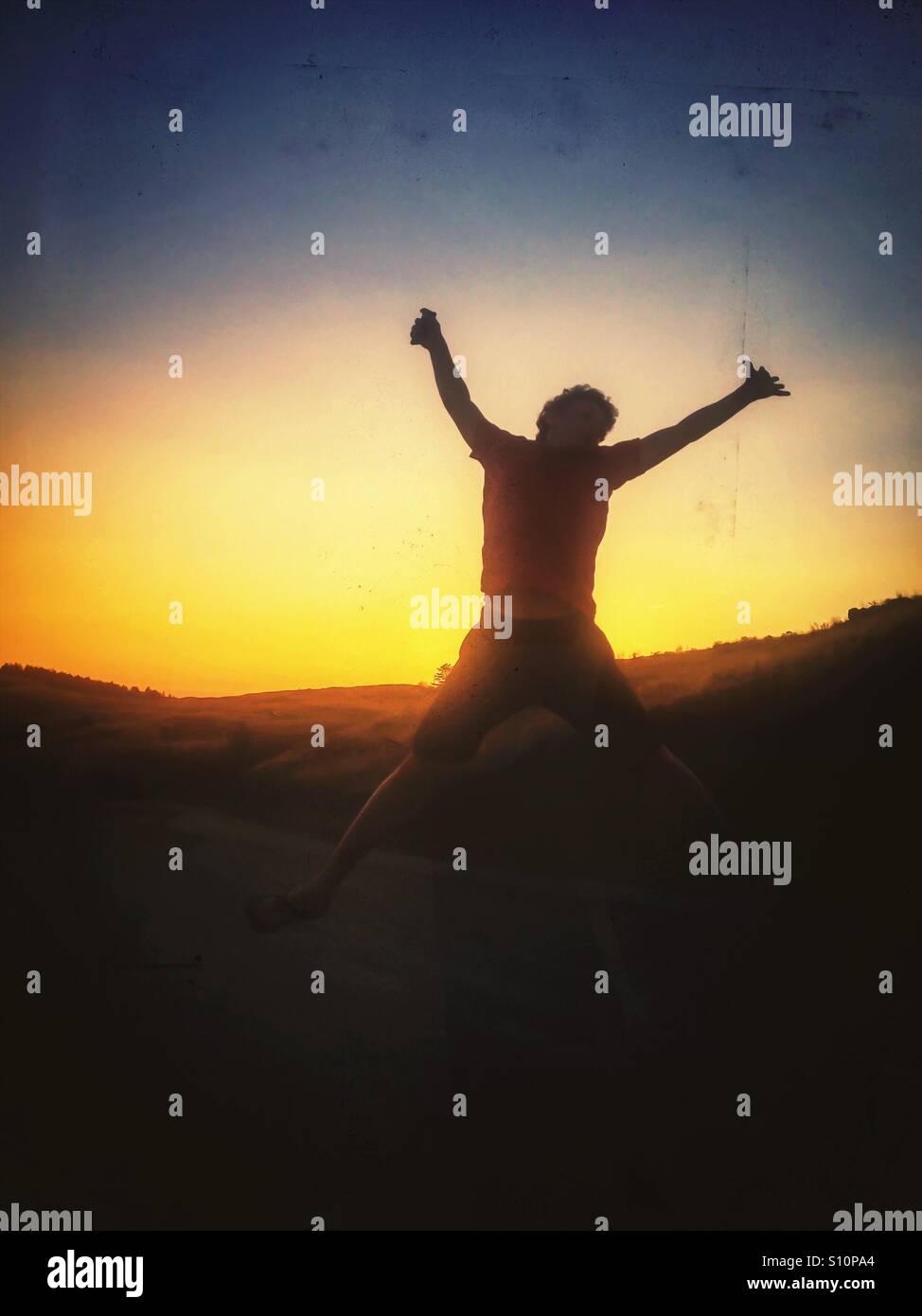 Jumping for joy at sunset. Teenage boy jumping in the air with arms up ...