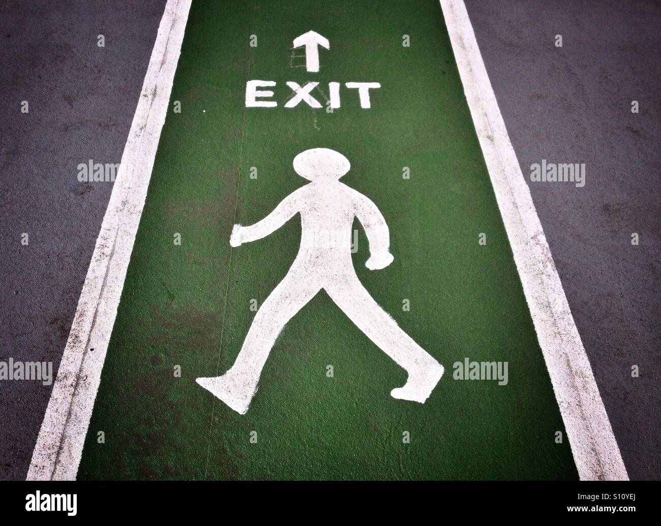An exit sign showing a walking man painted on the concrete floor of a ...