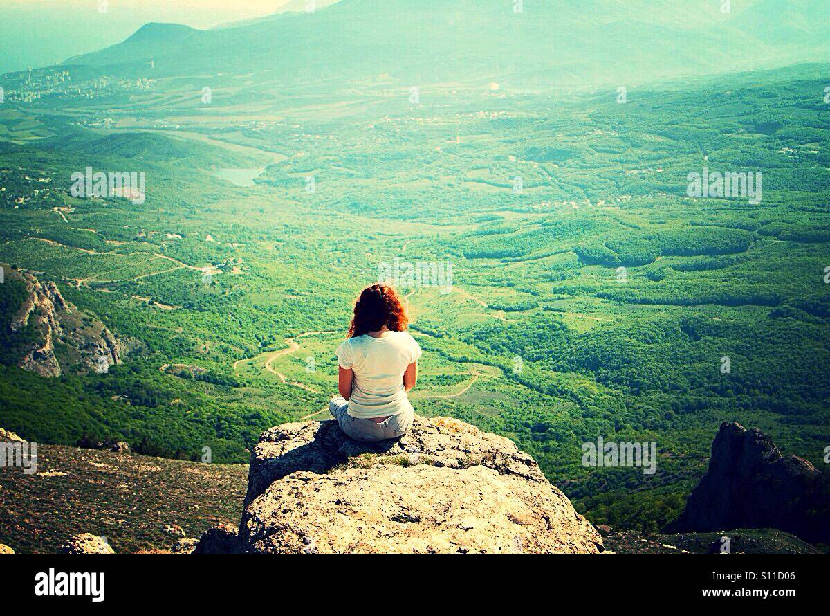 Girl sitting on the rock at the mountain top and looking forward Stock ...