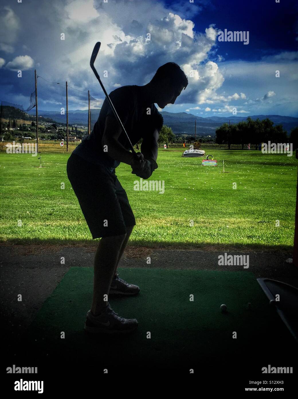 Silhouette of a young man hitting golf balls at a driving range on a ...