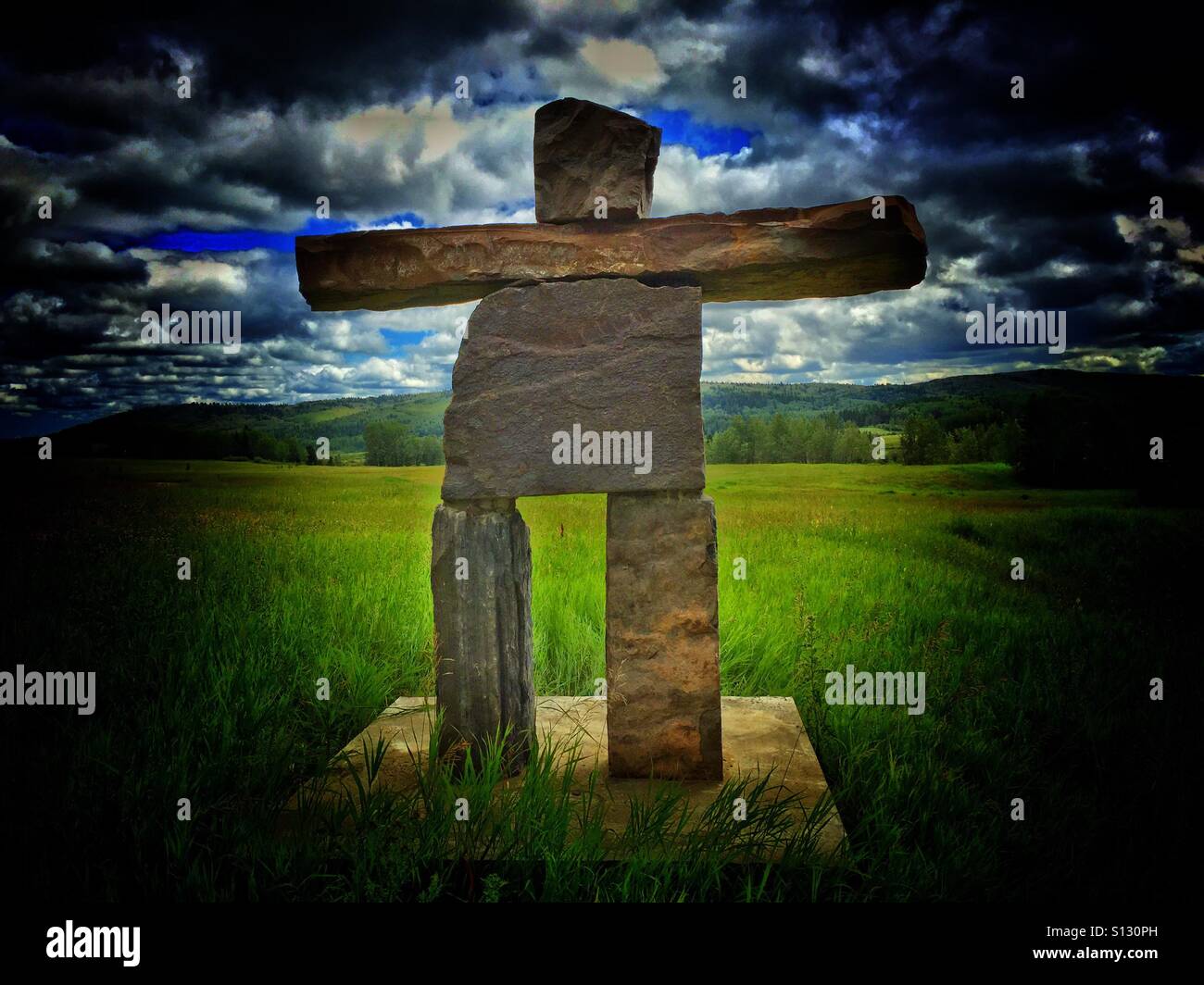 Unworked stone sculpture and a dramatic sky. An inuksuit or inukshuk is ...