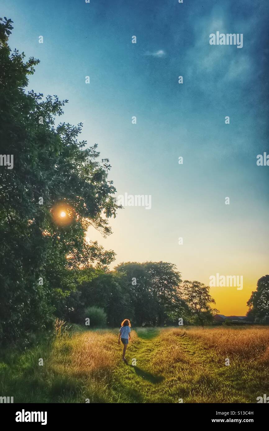 Young girl walking through field late in afternoon Stock Photo - Alamy