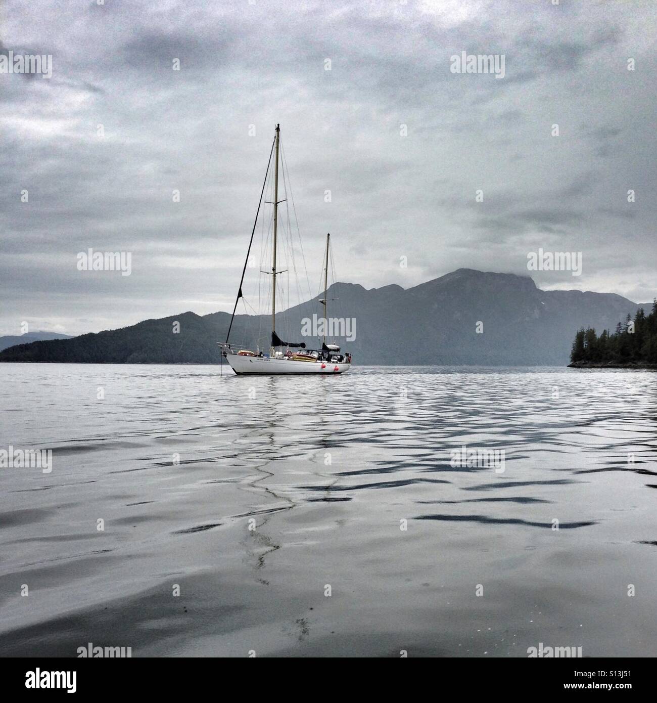 A ketch-rigged sailboat floats along the coast of British Columbia ...