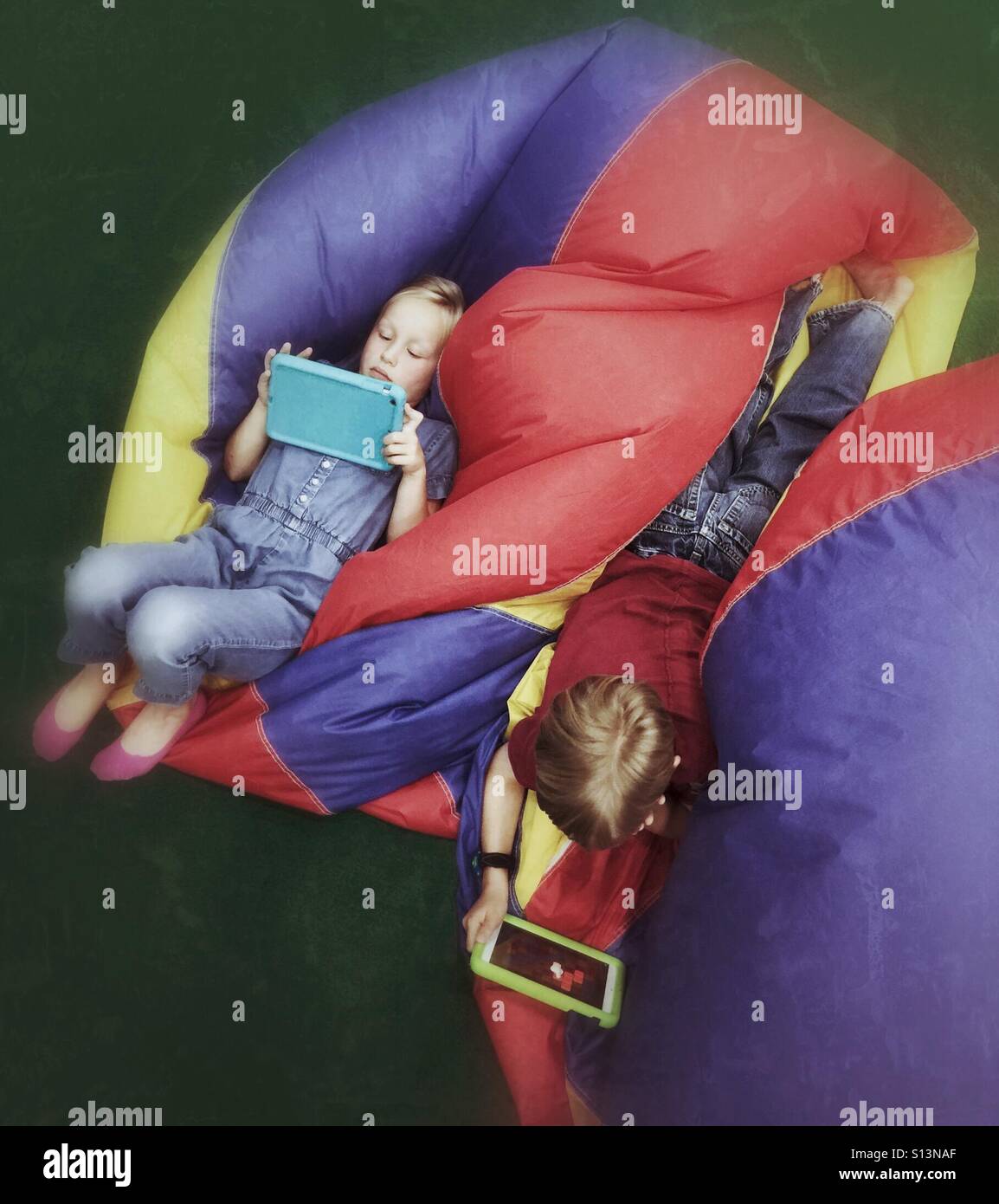 An overhead view of two children having screen time while relaxing on ...