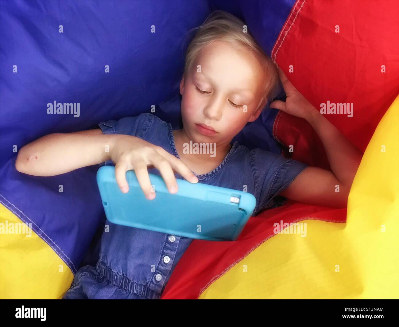A child relaxes on a deflating primary-coloured ball to play with a ...