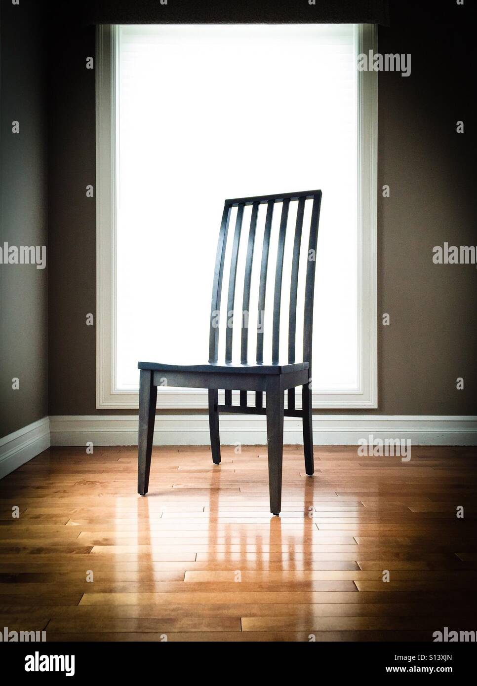 Light diffused through a window lights a single chair in a room with a ...