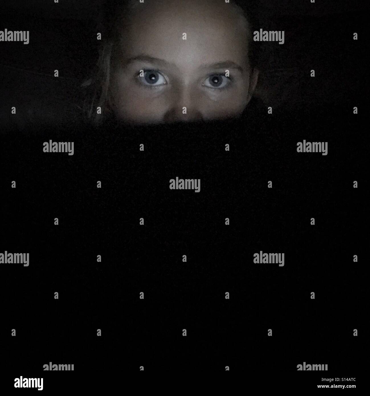 Child sat in the dark playing on her laptop, peering over the top of ...