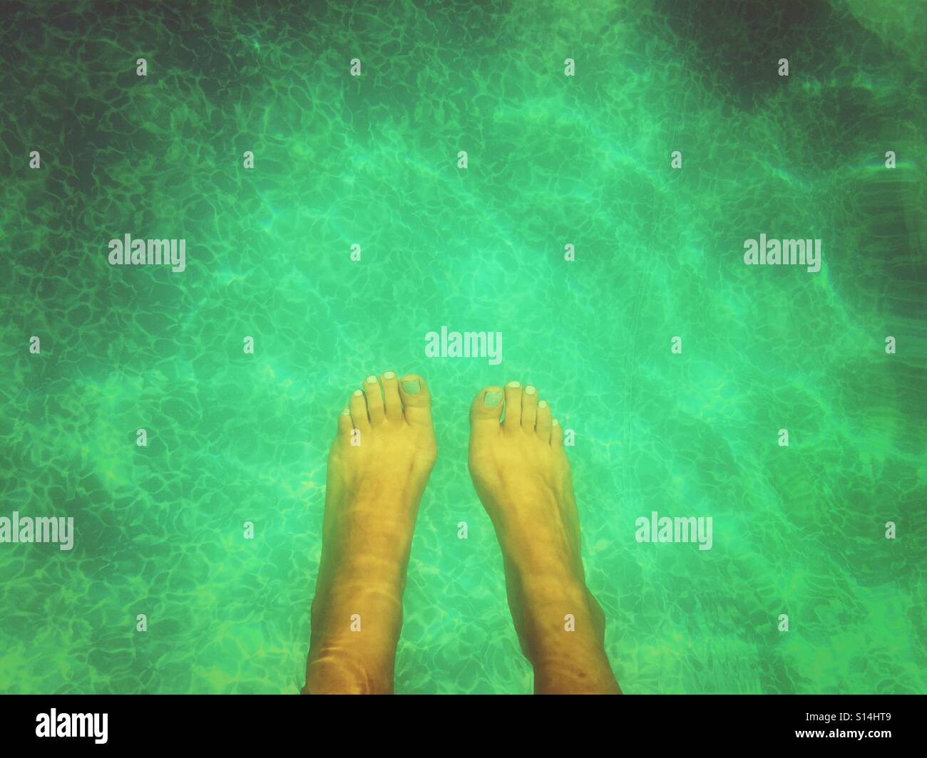Woman's feet submerged in swimming pool, with sunlight shimmering on ...