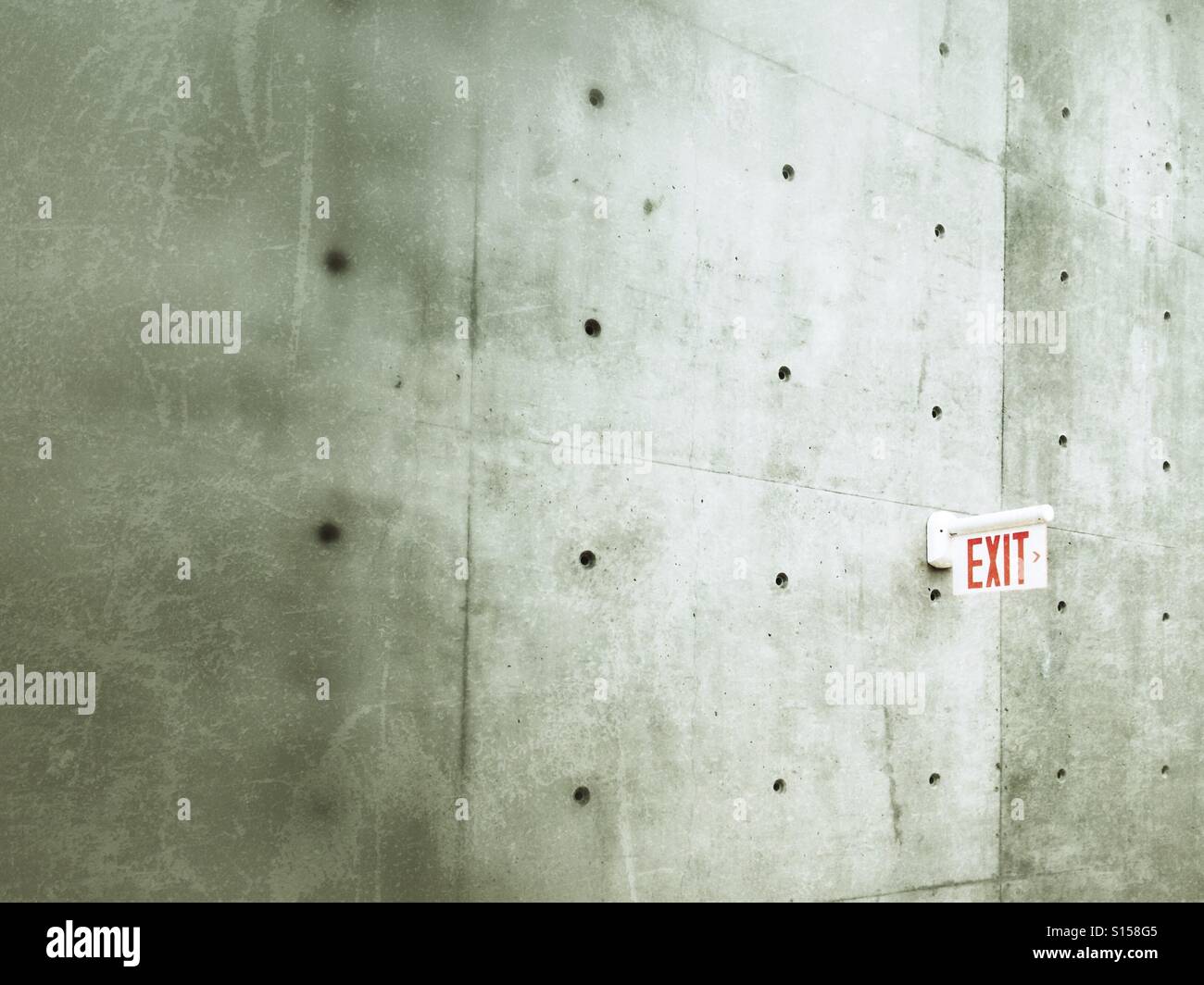 An exit sign hangs on a bare concrete wall Stock Photo - Alamy