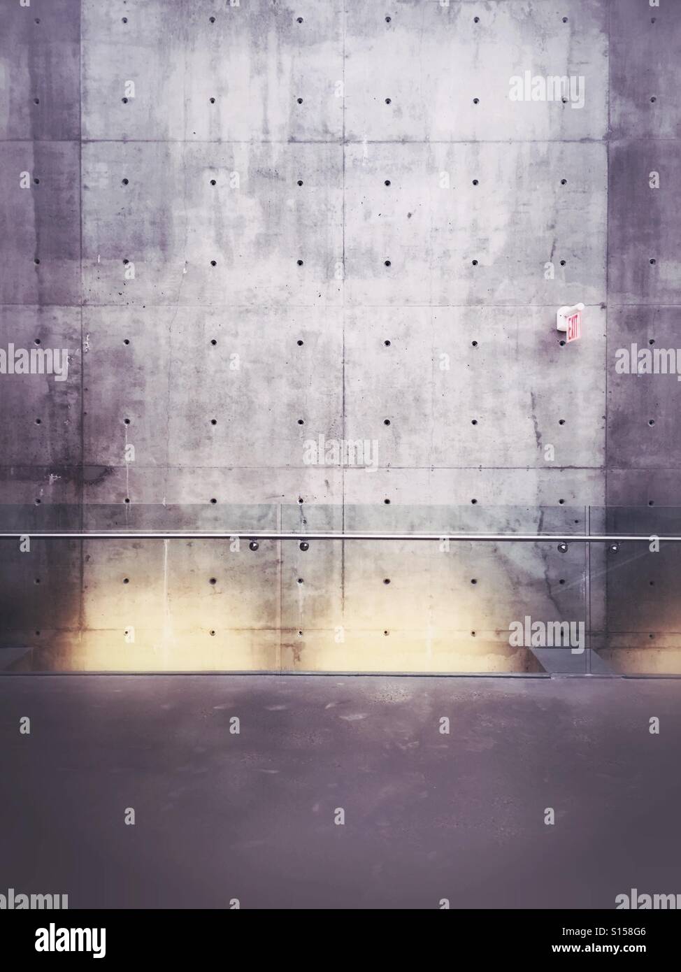 An exit sign hangs on a bare concrete wall behind a glass railing Stock ...