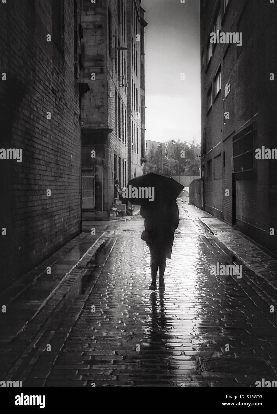 Woman with an umbrella walking along a cobbled lane when it was raining ...