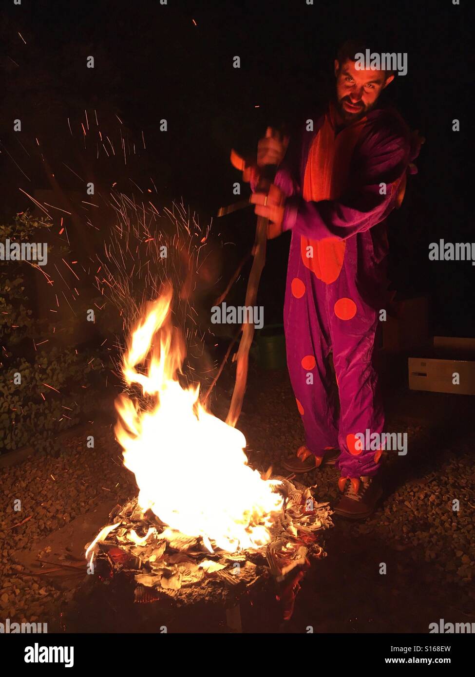 Man in monster/clown costume stokes a fire Stock Photo - Alamy