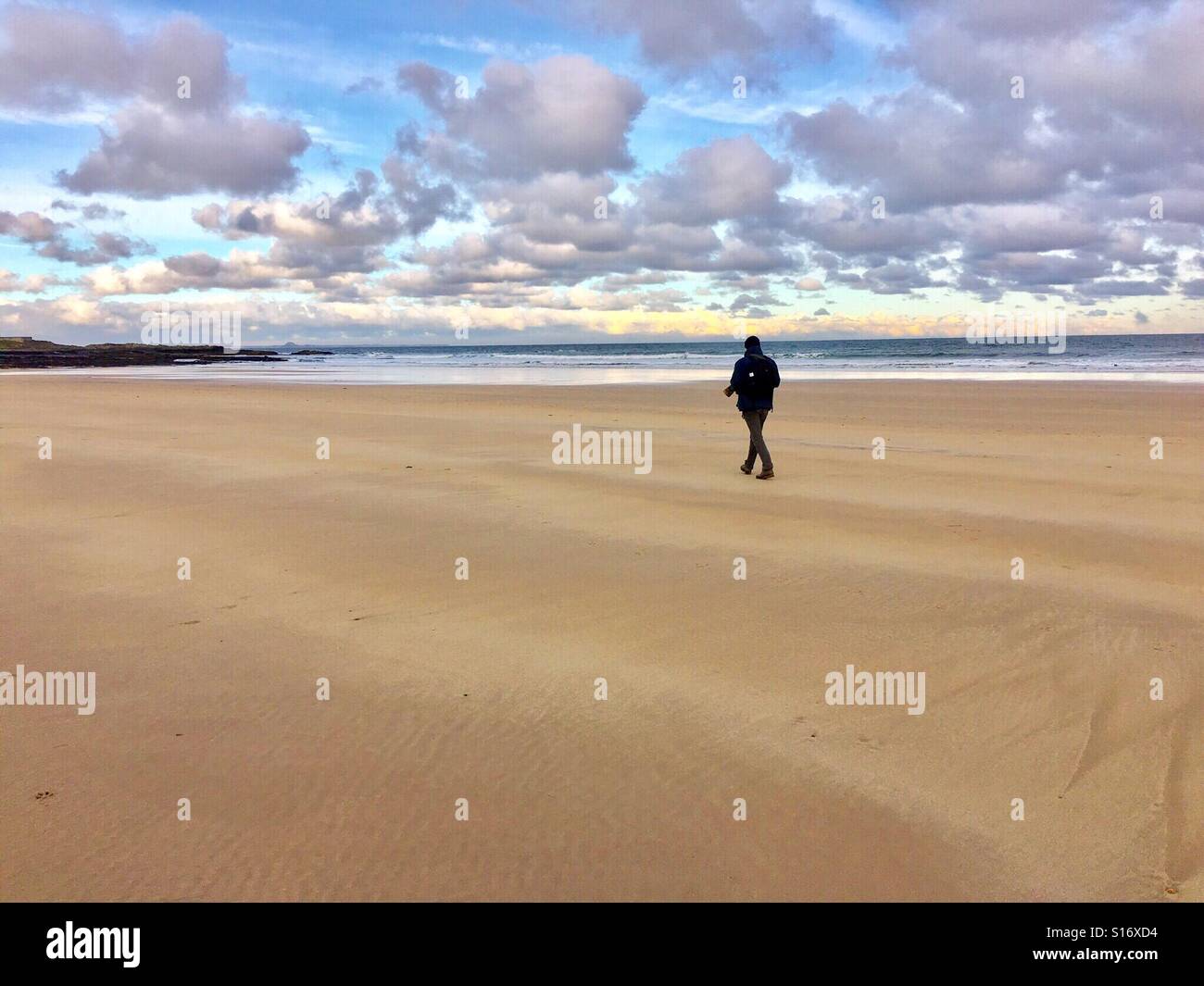 One man walking along a wide, sandy beach in winter Stock Photo - Alamy
