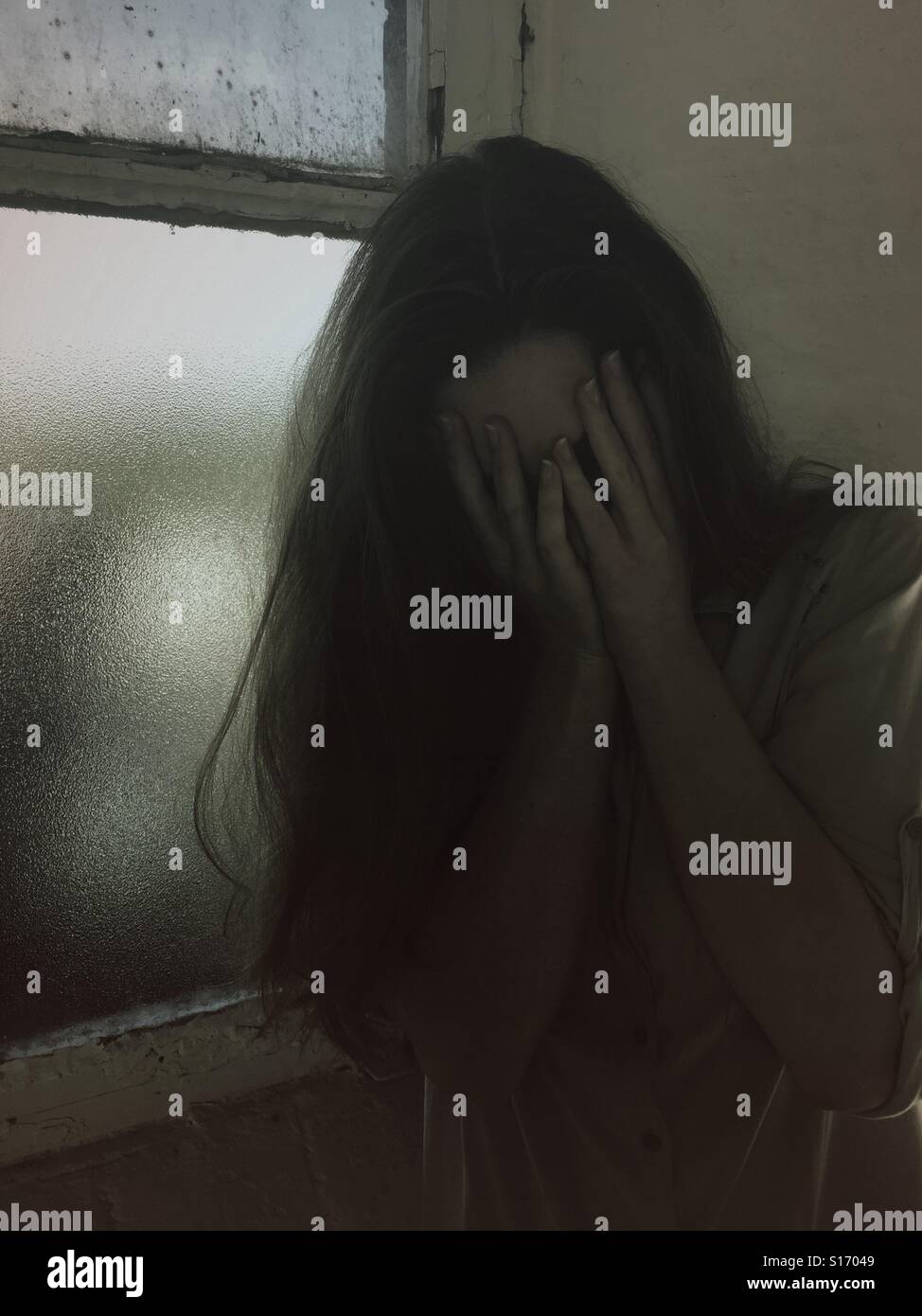 Woman hiding face with hands crying by the window Stock Photo - Alamy