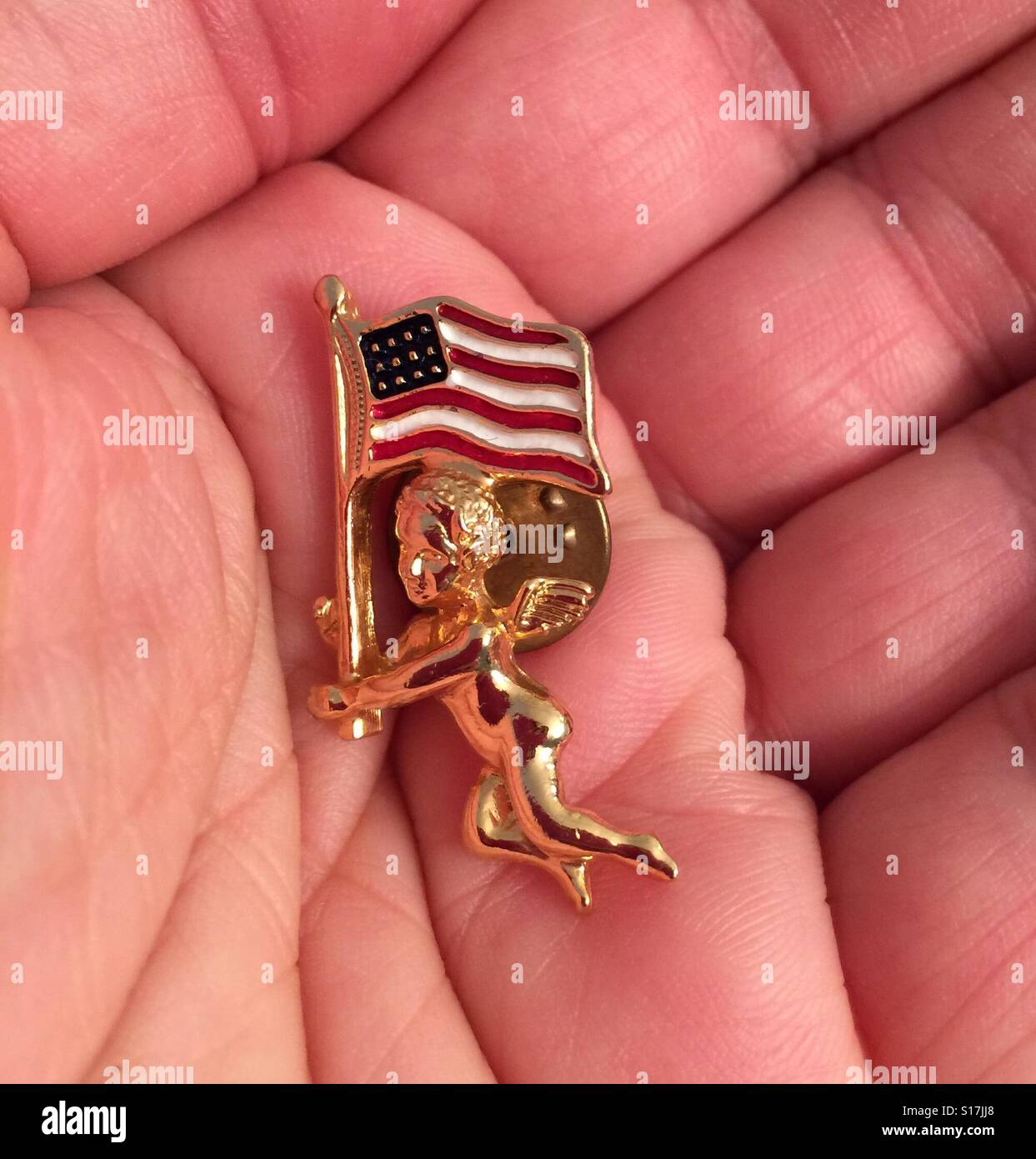 A Caucasian hand holding a golden angel pin with an American flag Stock ...