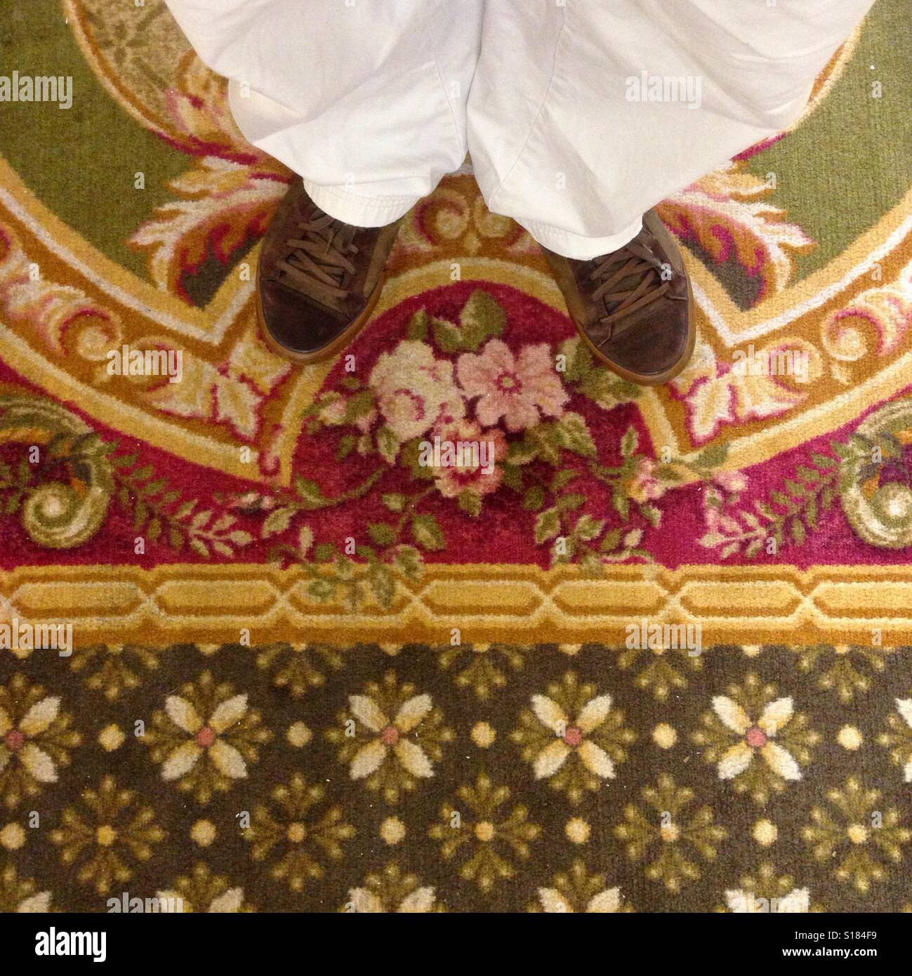 Legs and feet wearing sneakers on an ornate floral pattern carpet shot ...