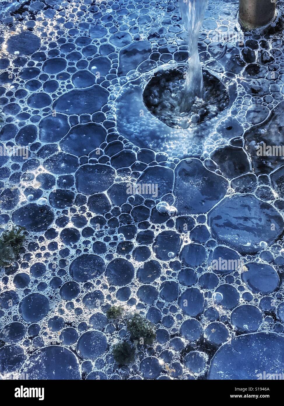 Air bubbles under the ice on a garden pond with the fountain running ...