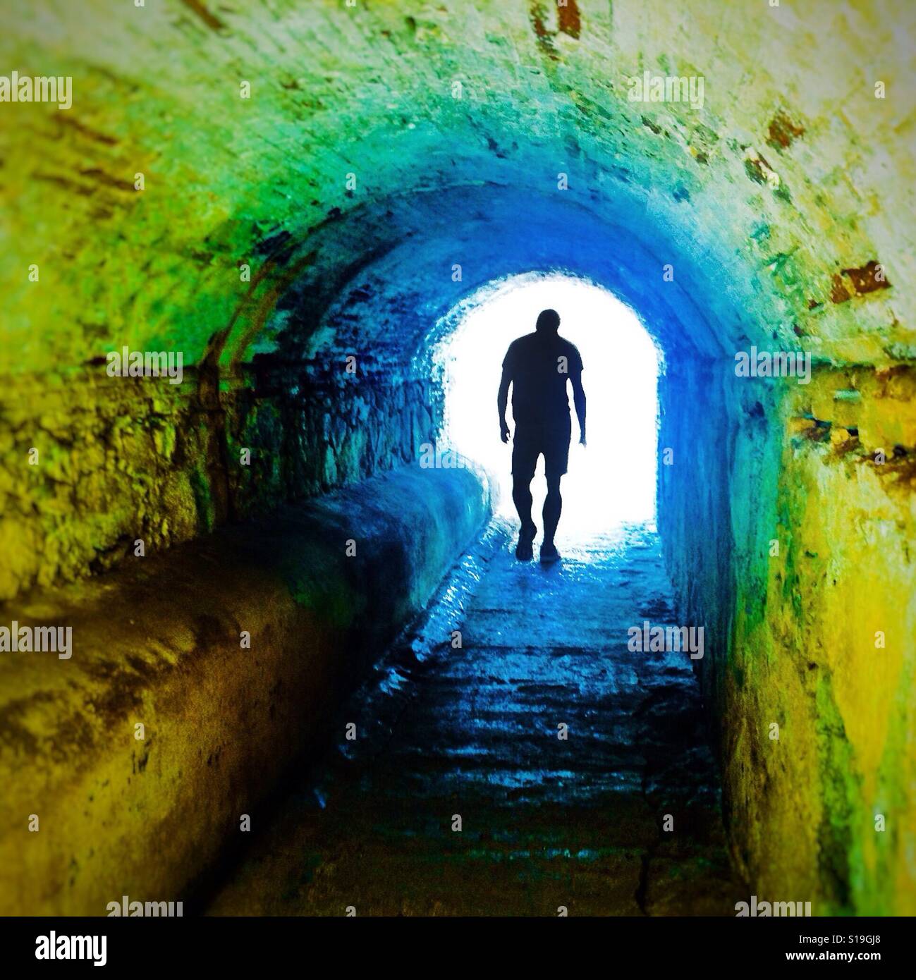 Anonymous silhouette of a person walking through a dark underpass ...