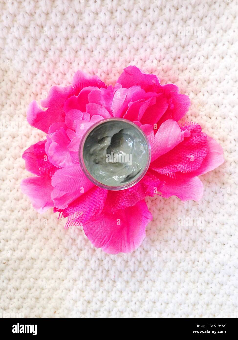 Clay facial mask in container sitting in centre of pink flower on white ...