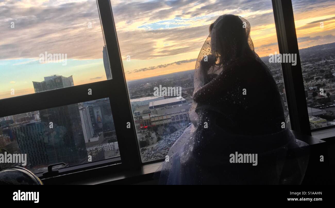 Young woman looks across Los Angeles skyline from skyscraper window at ...
