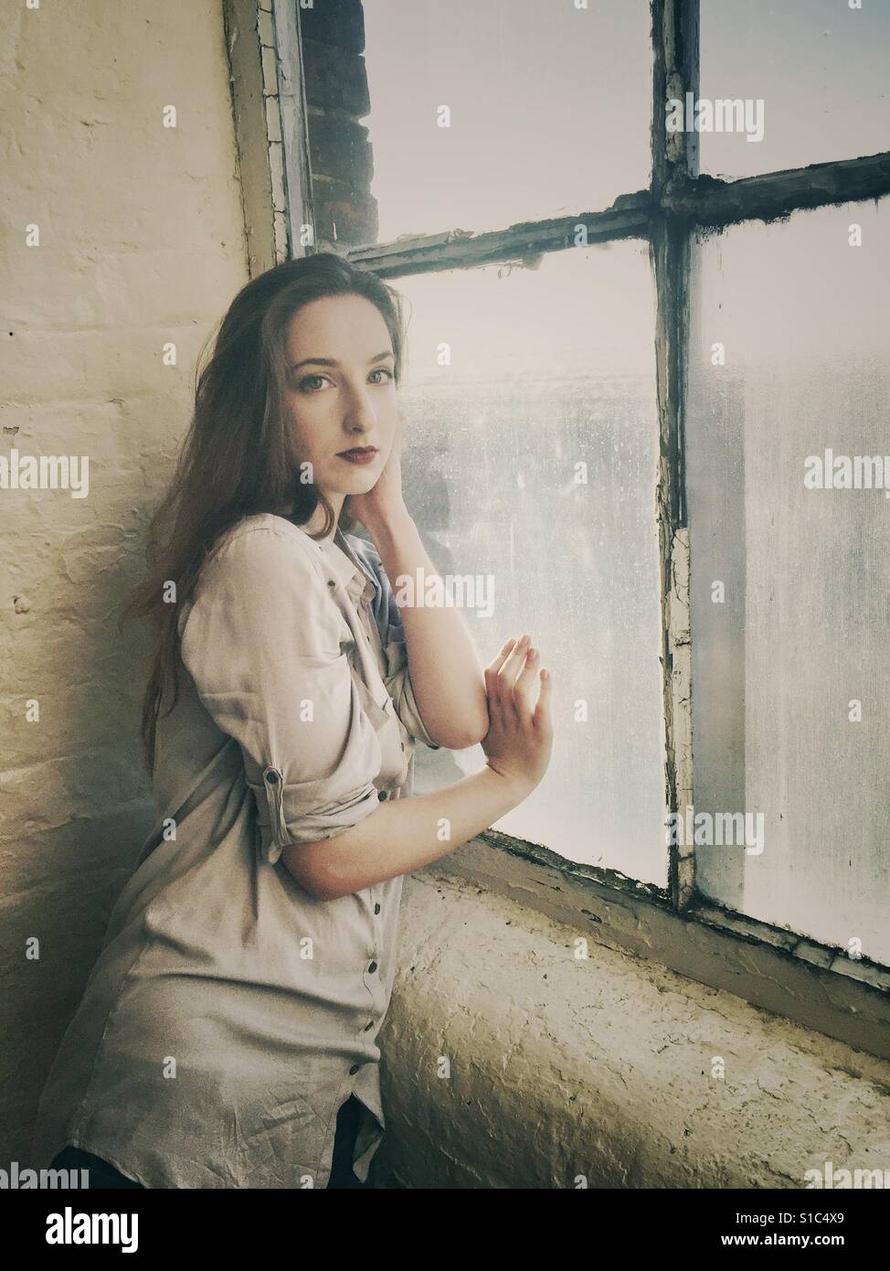 Beautiful young woman standing by the window Stock Photo - Alamy