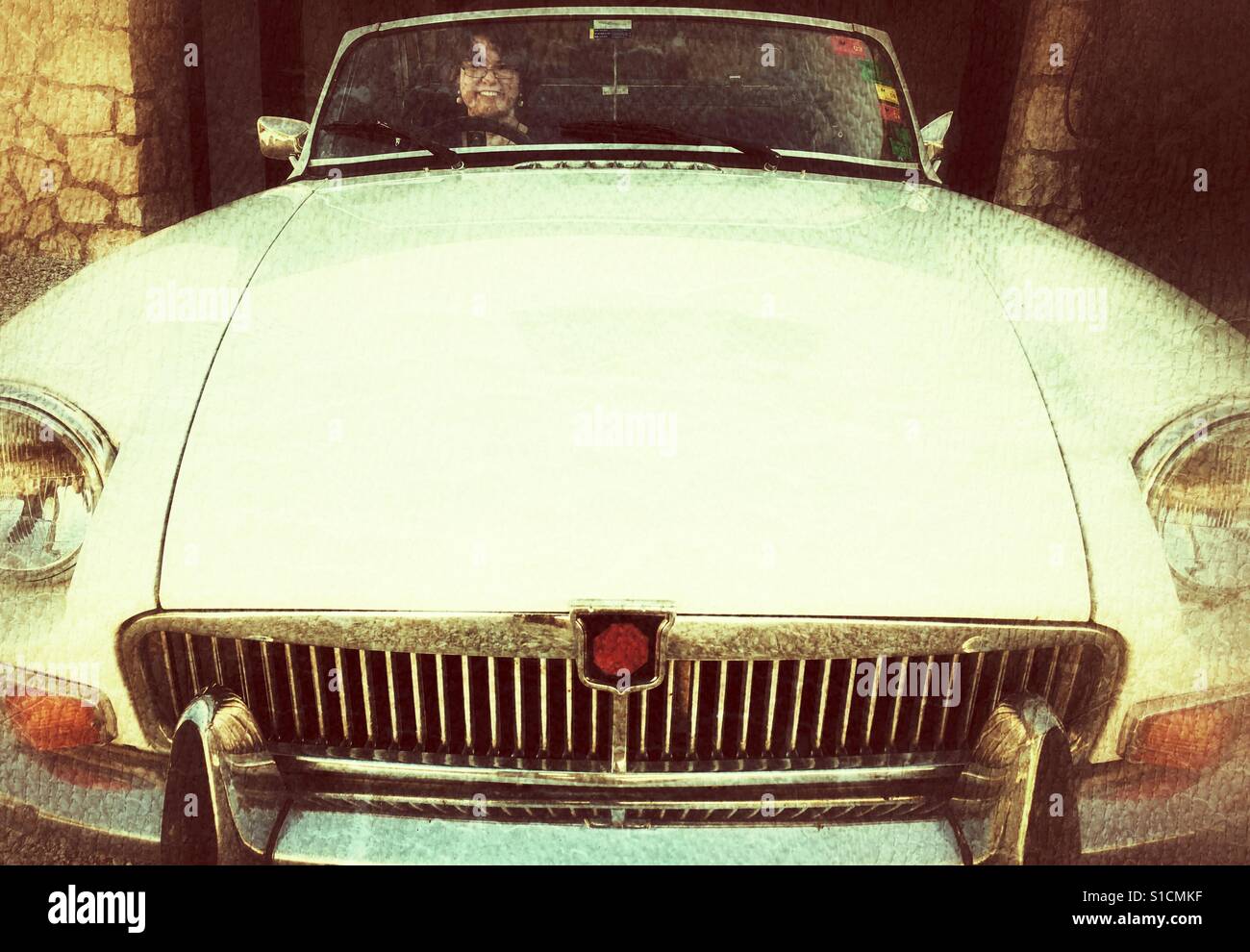 Young woman driving a 1973 MGB roadster with the hood down, coming out ...