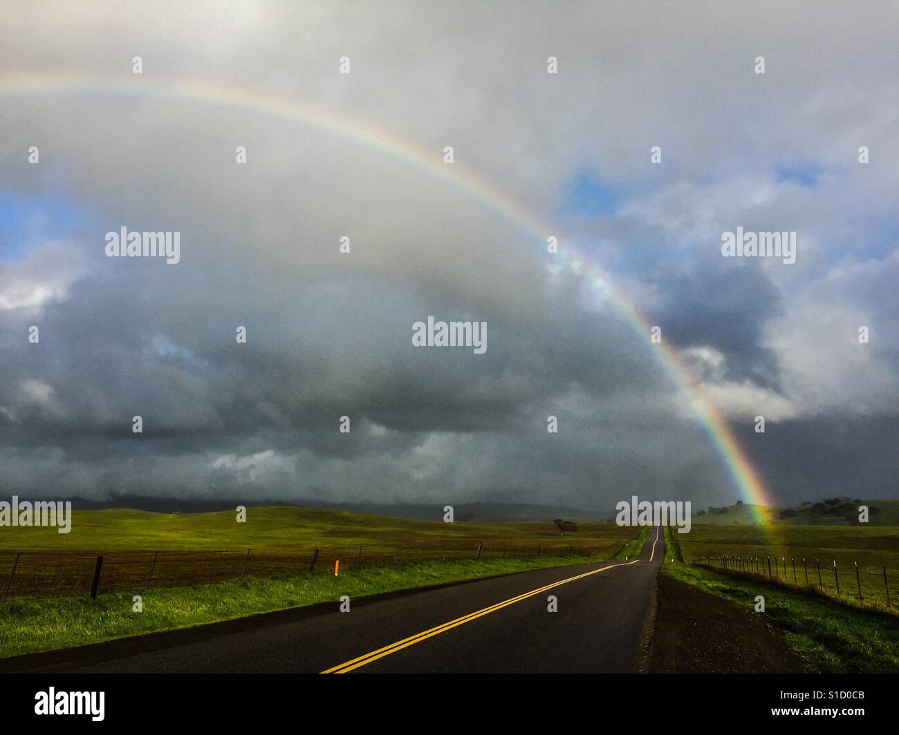 Rainbow over country road Stock Photo - Alamy