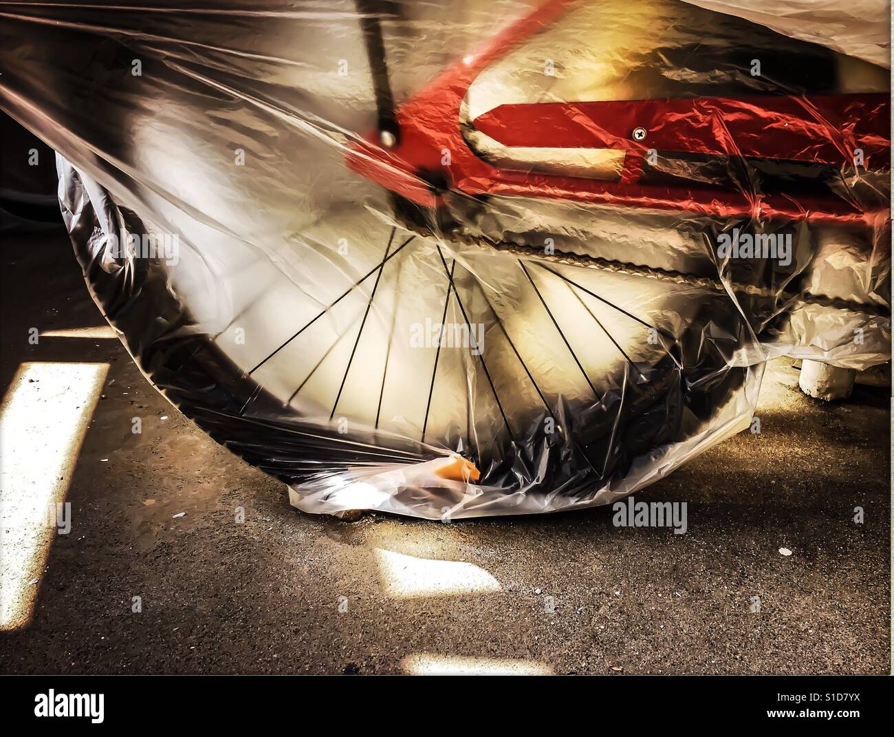 Bicycle wheel wrapped in plastic on red frame sunlight behind closeup ...