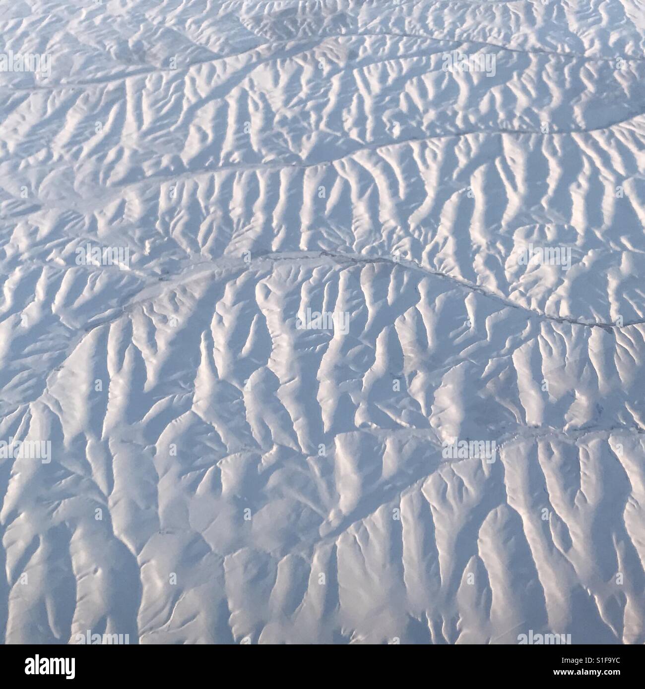 Snow covered land from an airplane shows the terrain of the land below ...