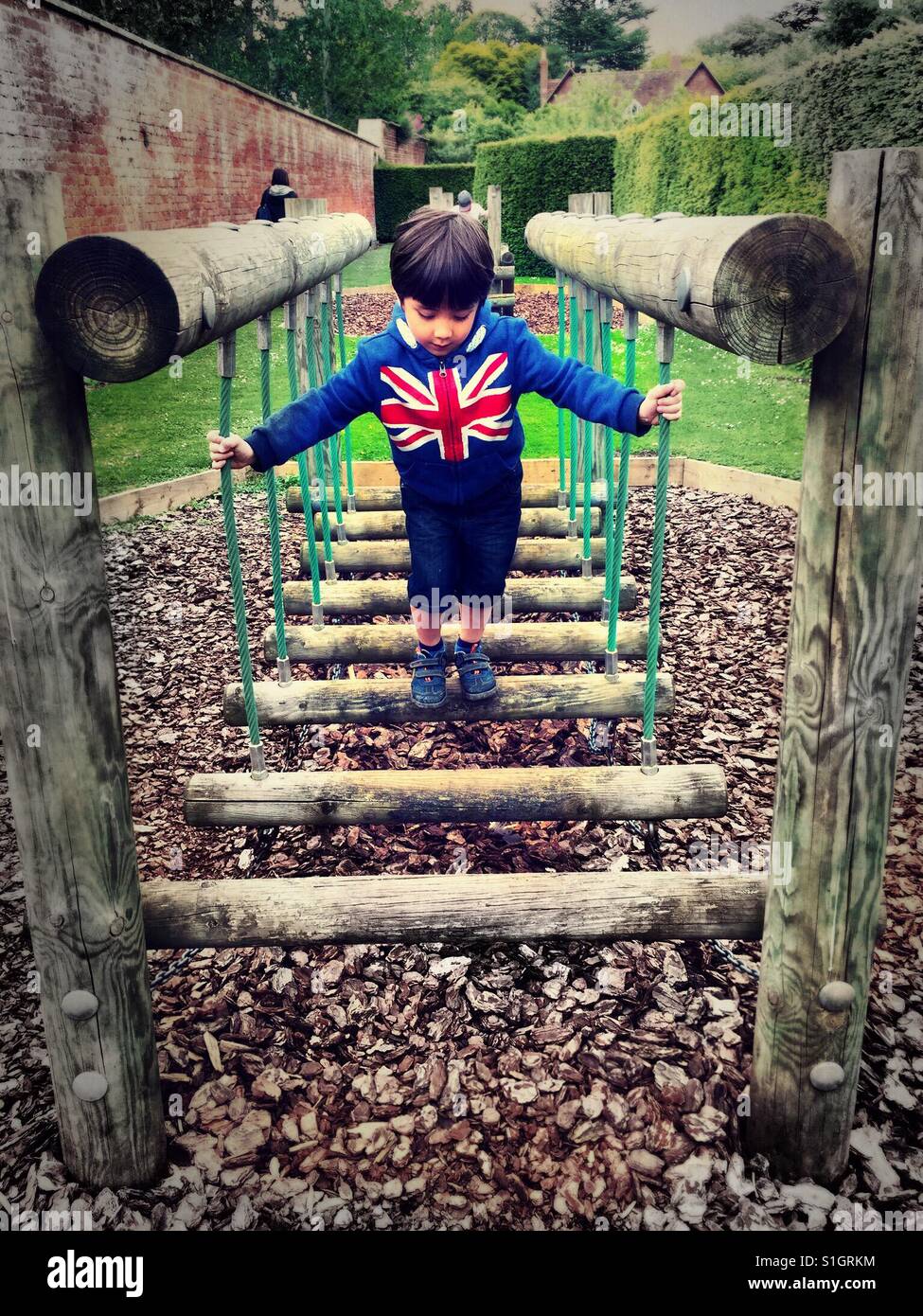 A young boy plays on a wooden bridge in a children's playground Stock ...