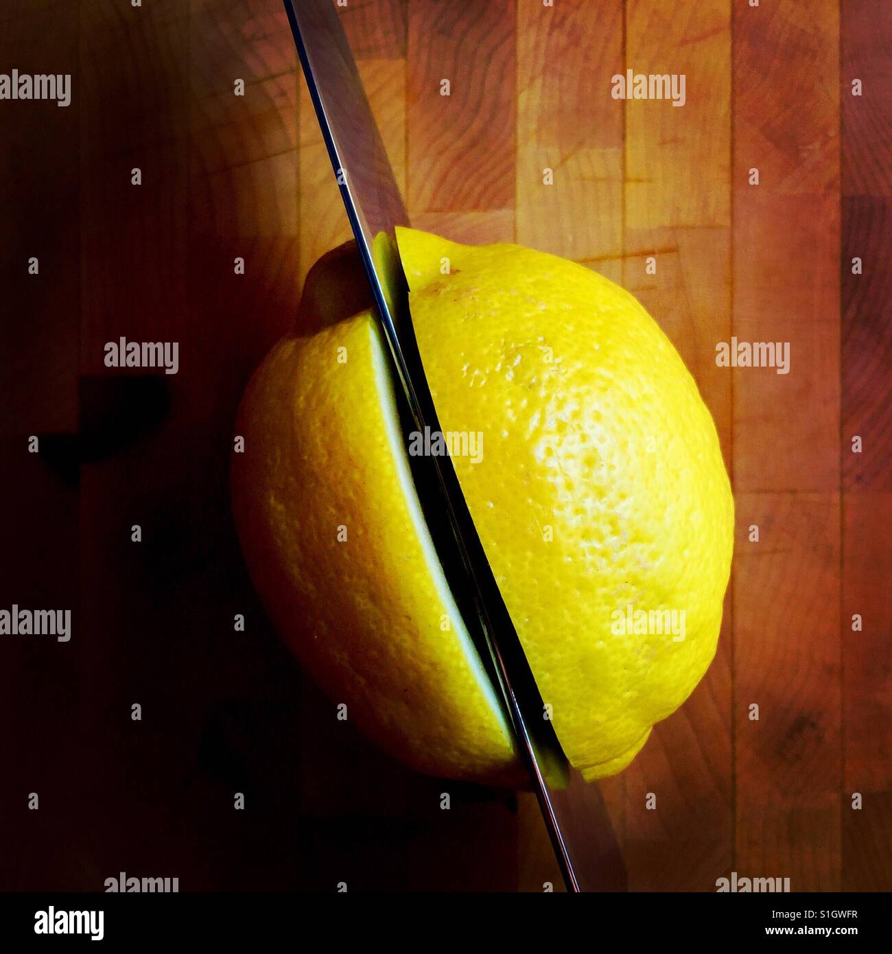 A fresh lemon being cut in half on a wood cutting board Stock Photo - Alamy