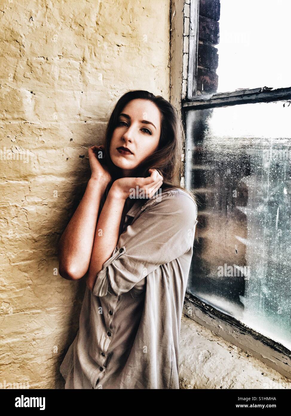 Beautiful young woman standing by the window Stock Photo - Alamy