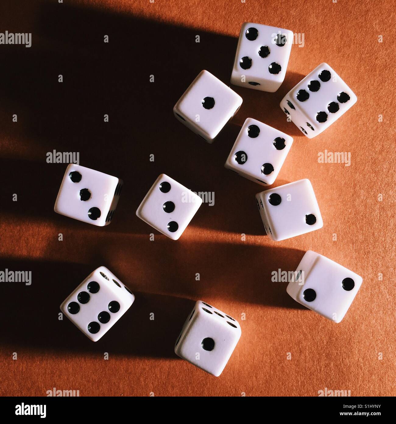 An overhead shot of 10 dice on a brown surface with heavy shadow Stock ...