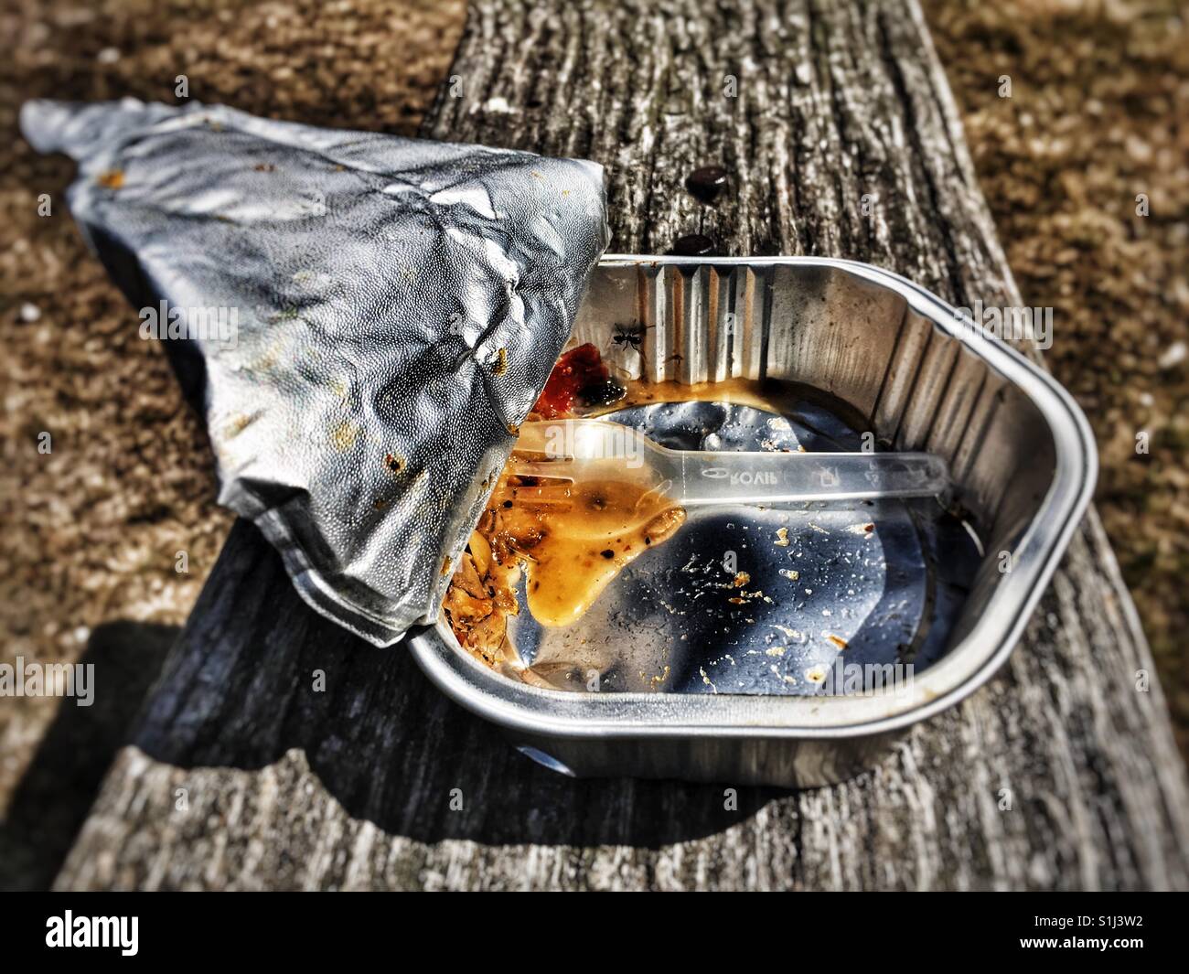 Take away food foil container left on park bench Stock Photo - Alamy