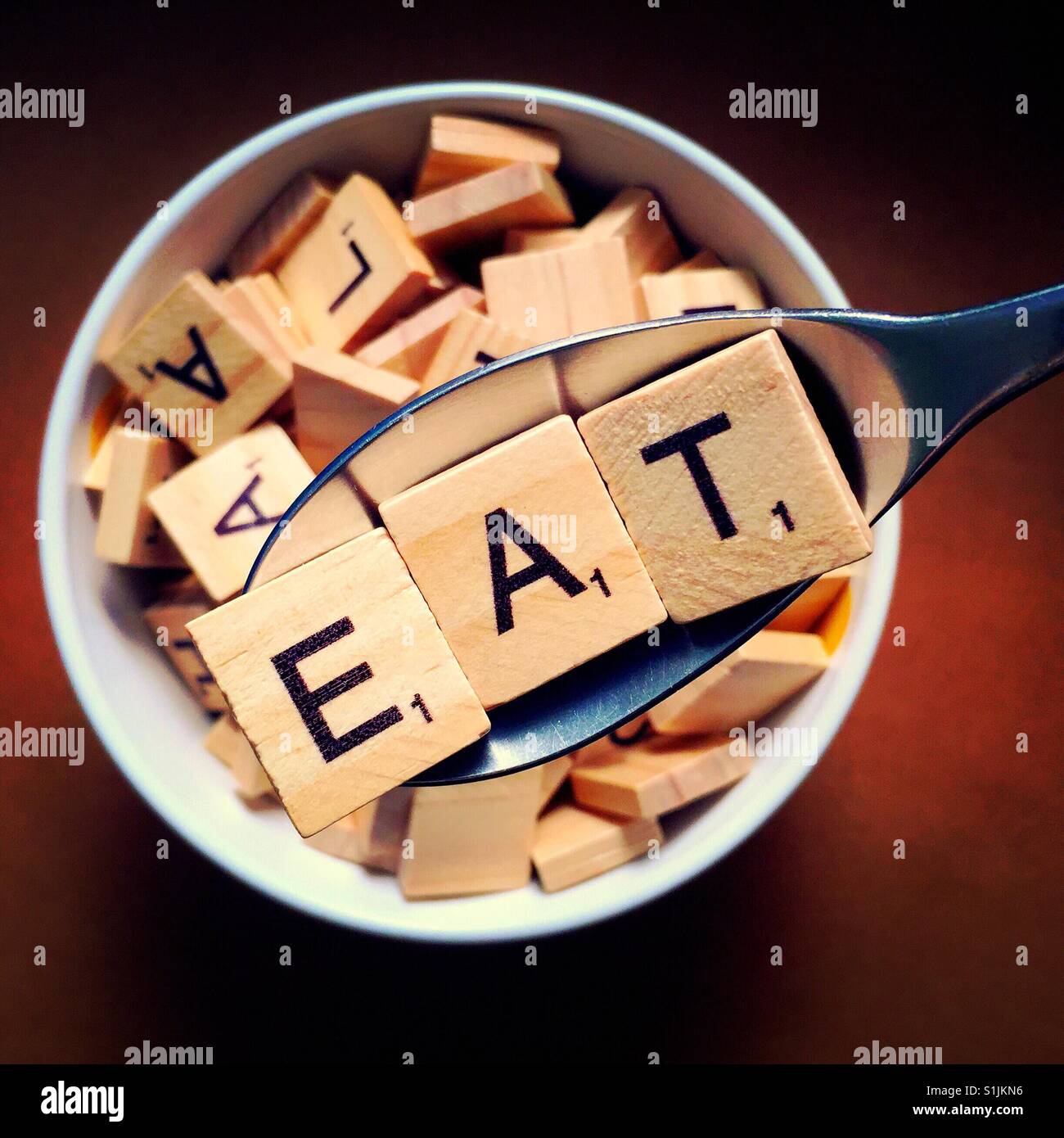 Close up of a spoon with wooden letters on it spelling out eat and a ...