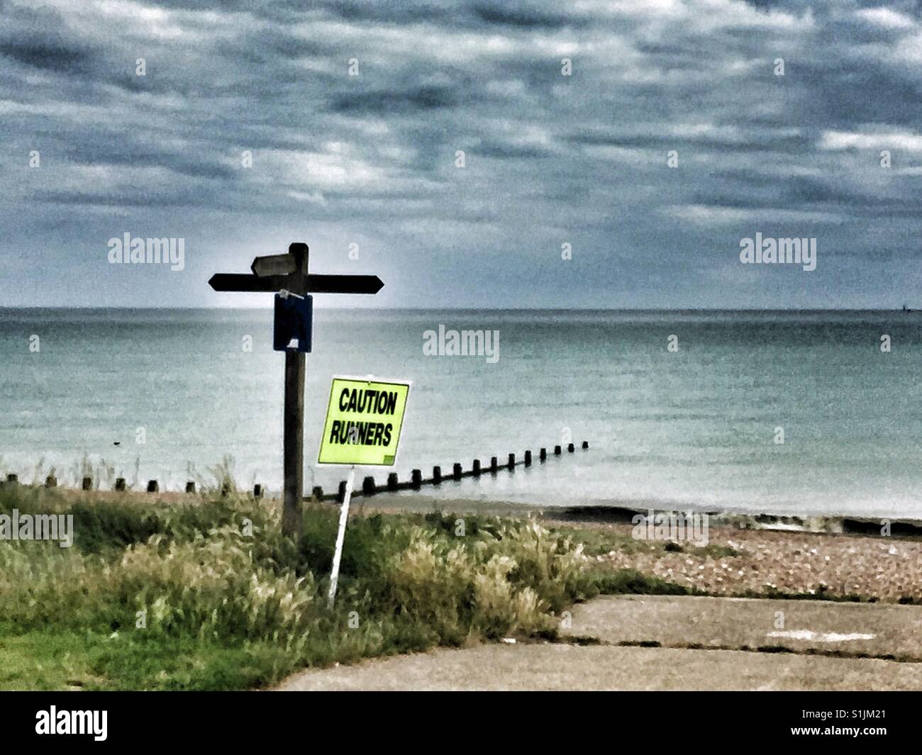 Caution runners sign alongside signpost showing footpath along seafront ...