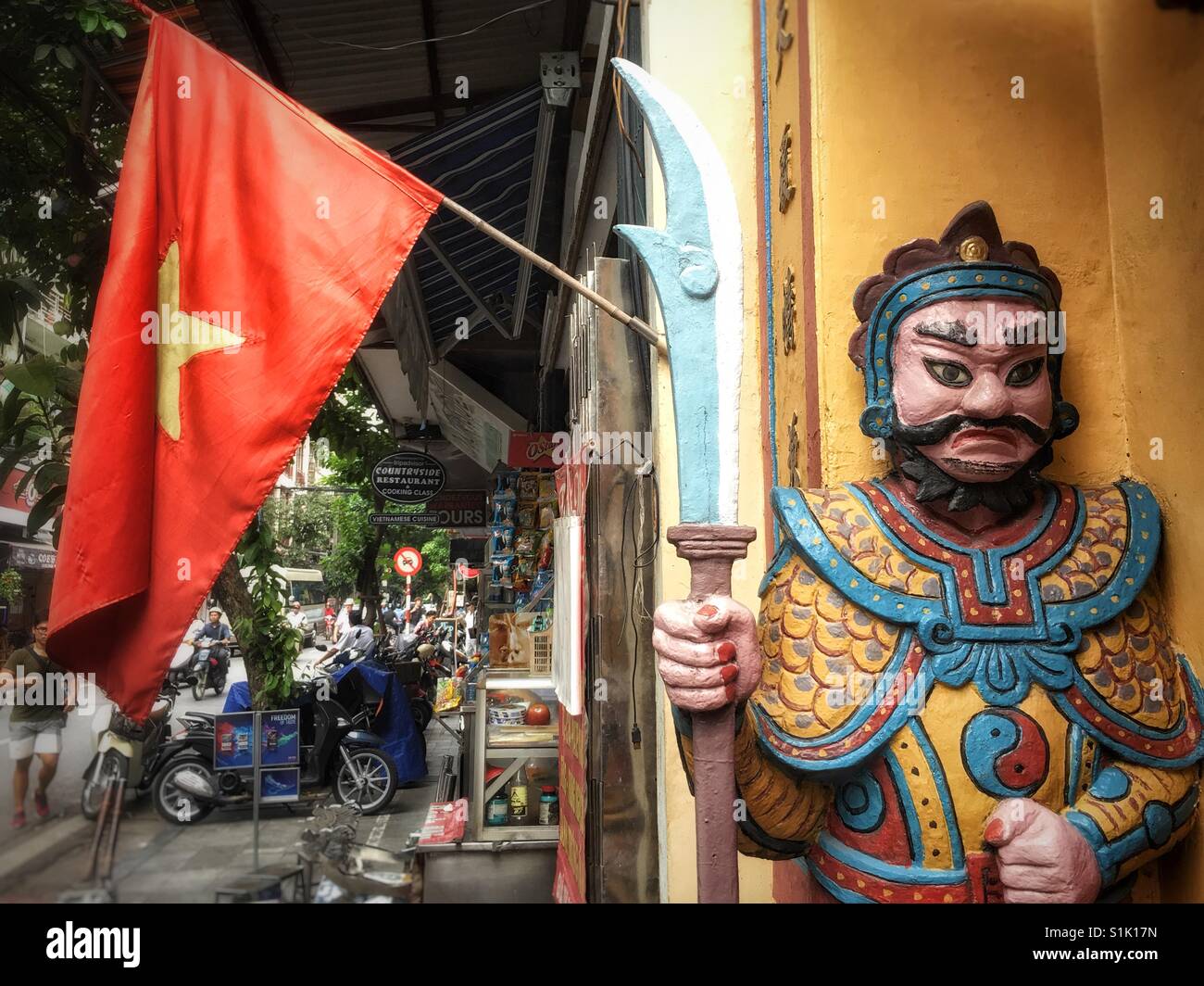 Ornate carved warrior statue and Vietnamese flag on a street in the Old ...