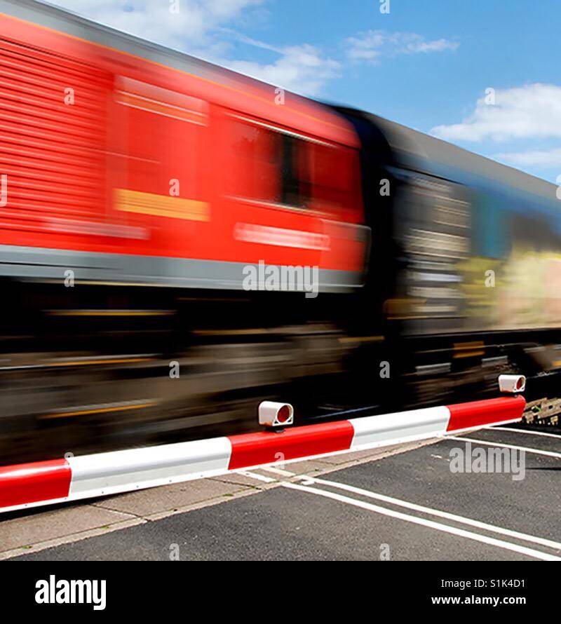 Fast freight train passing a railway crossing at speed, with motion ...