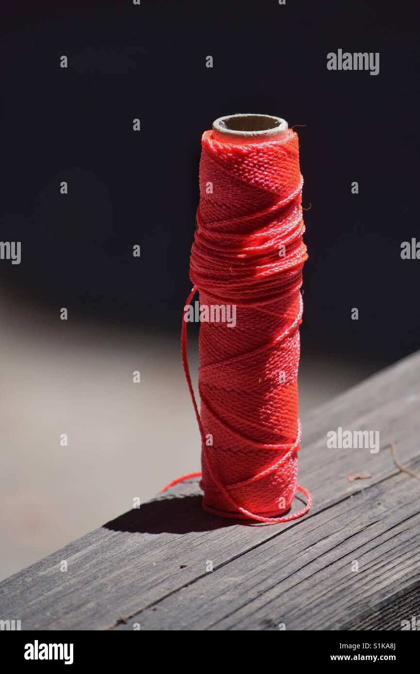 A bright red roll of kite string sits on a gray wooden deck railing ...