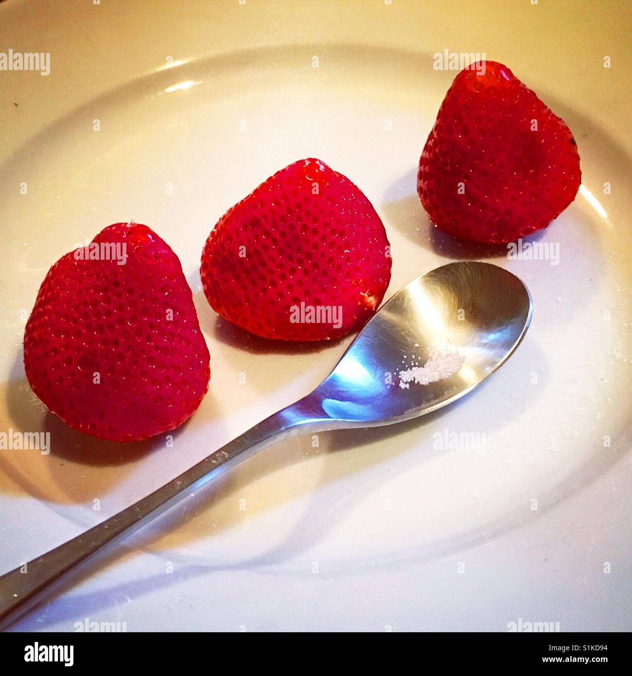 Three strawberries and a spoon. Mobile phone photo with some phone or ...
