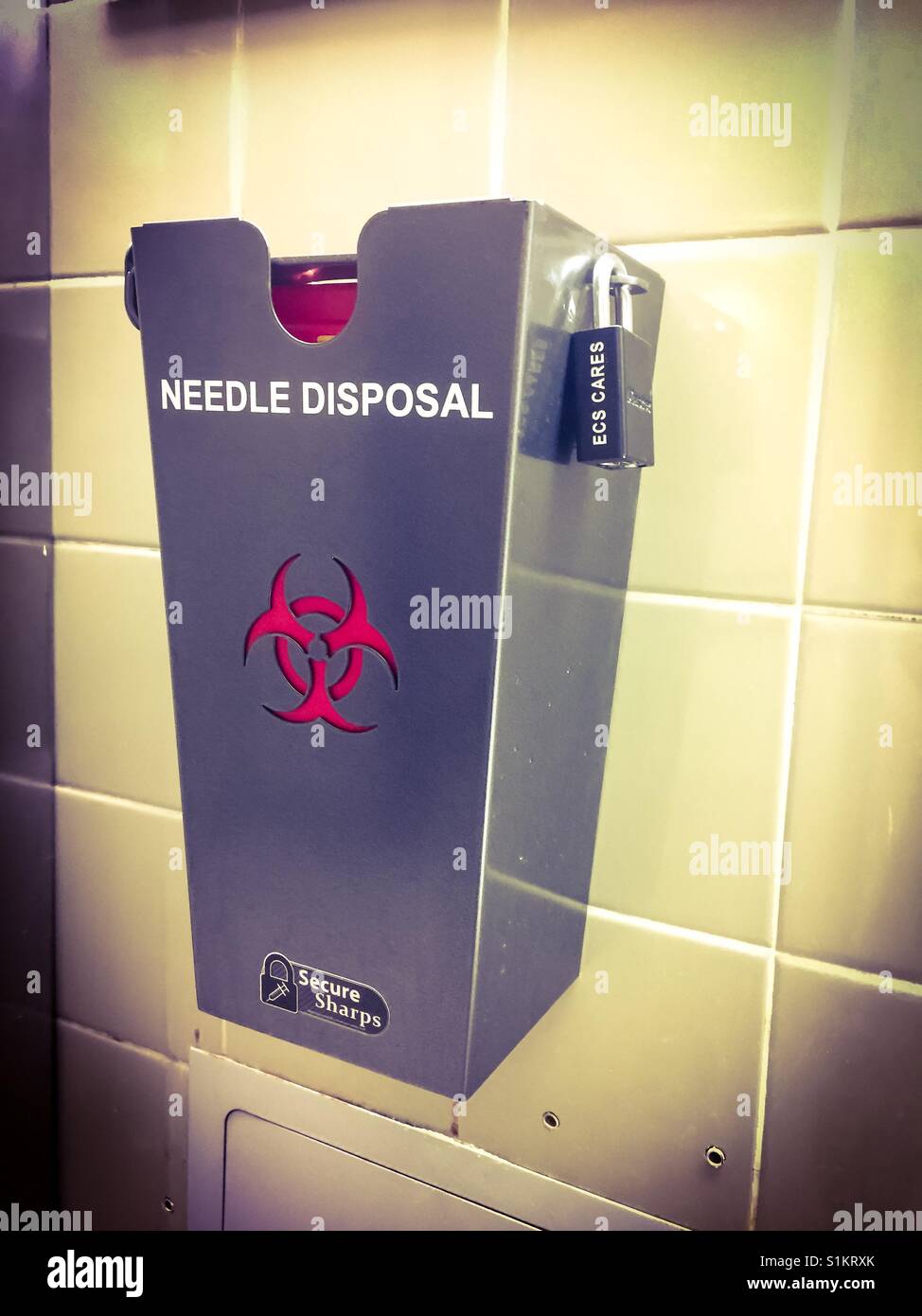Locked needle disposal box attached to a tiled wall in a public ...