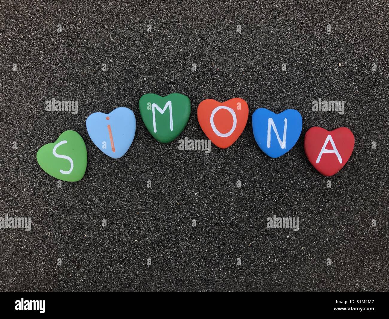Simona, feminine name with colored stone letters over black volcanic ...