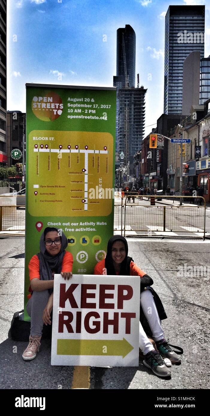 Two young girls holding a directional sign during a street festival ...